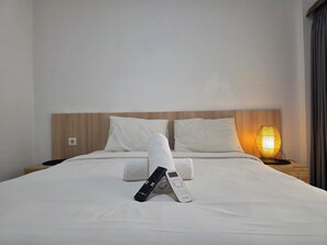 Cama bem arrumada com lençóis brancos, duas almofadas e um controle remoto sobre a cama.
