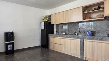 Cozinha moderna com bancada de mármore, armários de madeira e geladeira preta, além de um dispenser de água.