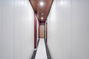 Um corredor com paredes brancas, chão de mármore e teto de madeira.