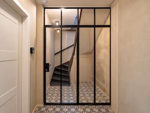 Um corredor com piso de azulejos que leva a uma escadaria com corrimão preto.