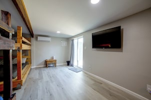 Quarto com beliche de madeira, televisão de tela plana na parede e janela com cortinas.