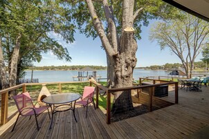 Um deck de madeira com mesa e cadeiras, com vista para um lago que inclui um gazebo e um píer.