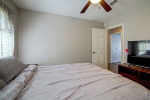 Quarto com uma cama, televisão sobre um suporte de madeira e porta que dá para outro cômodo.