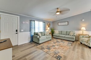 Sala de estar com sofá, tapete estampado, ventilador de teto e placa na parede.