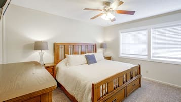 Quarto com cama de madeira, duas mesas de cabeceira, ventilador de teto e janela com persianas.
