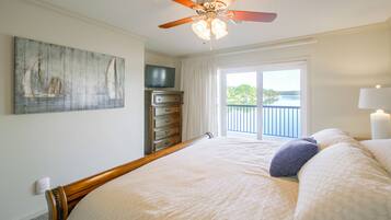 Quarto com cama, ventoinha no teto, cômoda, televisão e janela com vista para uma varanda.