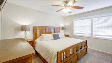 Quarto com cama de madeira, duas mesas de cabeceira, ventilador de teto e janela com persianas.