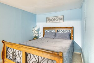 Quarto com estrutura de cama de madeira, colcha cinza e placa na parede com a inscrição 'Lar Doce Lar'.