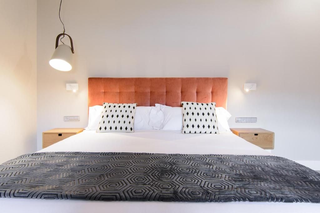 Cama bem arrumada com colcha estampada, cabeceira acolchoada e luminárias nas mesas de cabeceira de madeira.