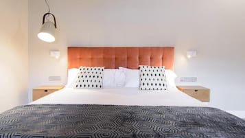 Cama bem arrumada com colcha estampada, cabeceira acolchoada e luminárias nas mesas de cabeceira de madeira.