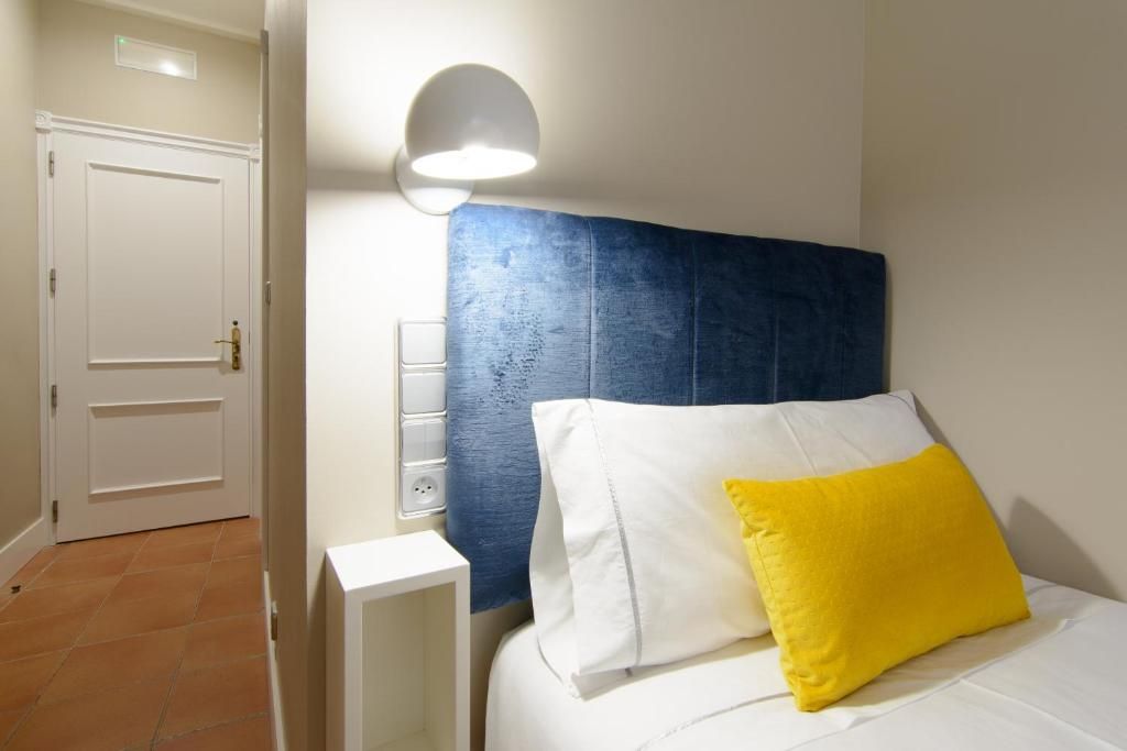 Quarto de hotel com cama, mesa de cabeceira, luminária na parede e porta.