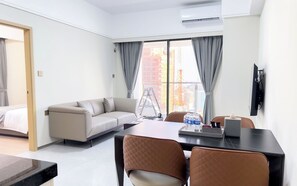 Quarto de hotel com sofá, mesa de jantar com cadeiras, televisão fixada na parede e janela com cortinas.
