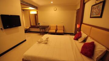 Quarto de hotel com cama, escrivaninha, cadeira, televisão e relógio na parede.