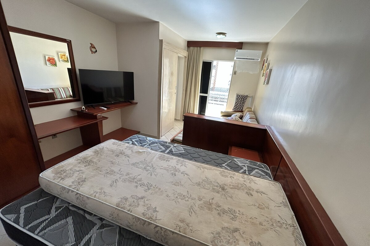 Quarto de hotel com cama, televisão, escrivaninha e janela.