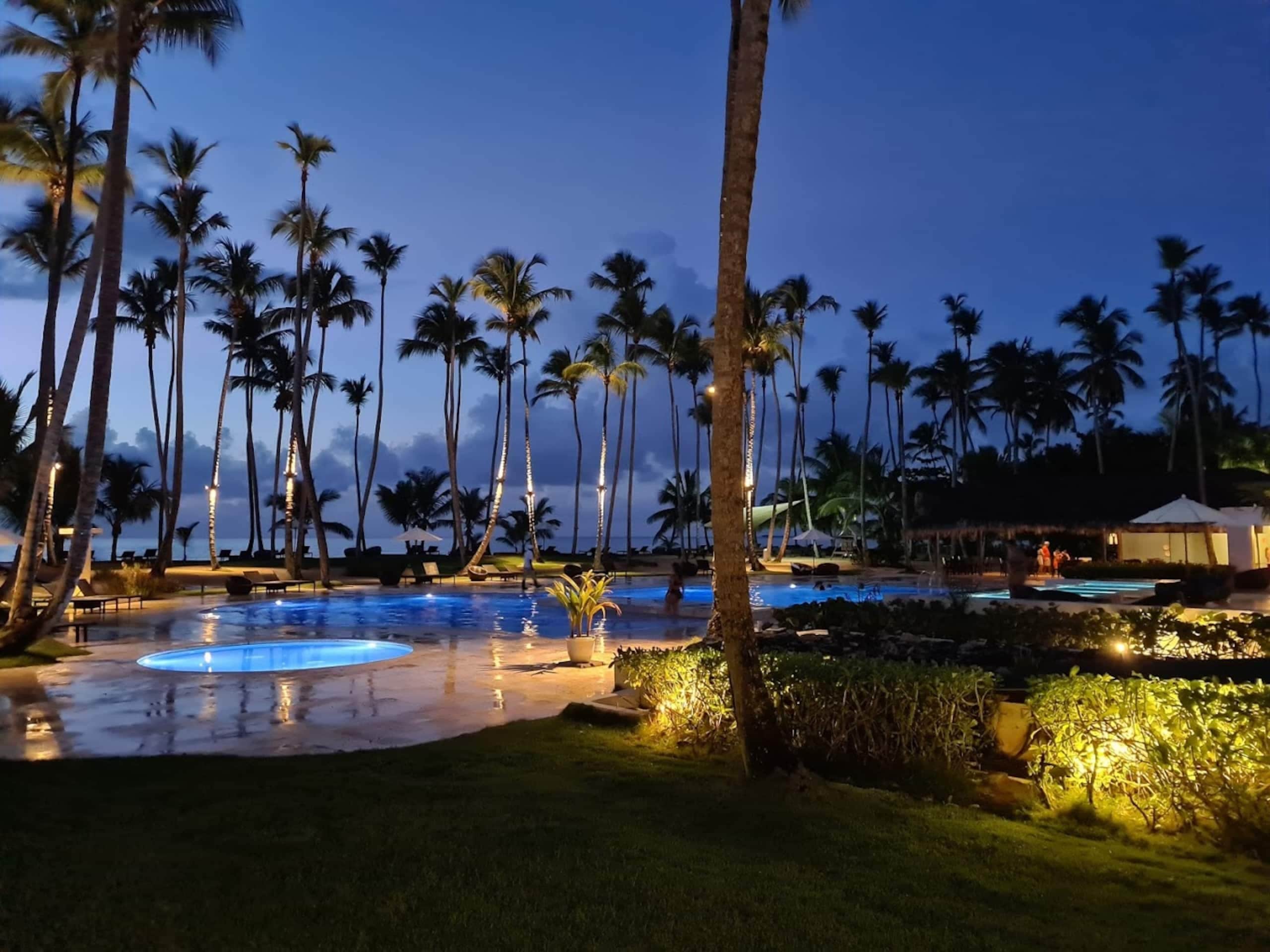Uma área de piscina em resort, com várias piscinas, palmeiras e espreguiçadeiras.