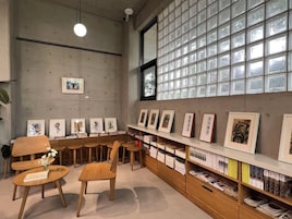 Uma biblioteca com estantes, obras de arte emolduradas e cadeiras de madeira.