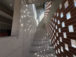 Uma escadaria com design moderno, apresentando uma parede de tijolos com recortes quadrados no lado direito e uma parede de concreto lisa no lado esquerdo.