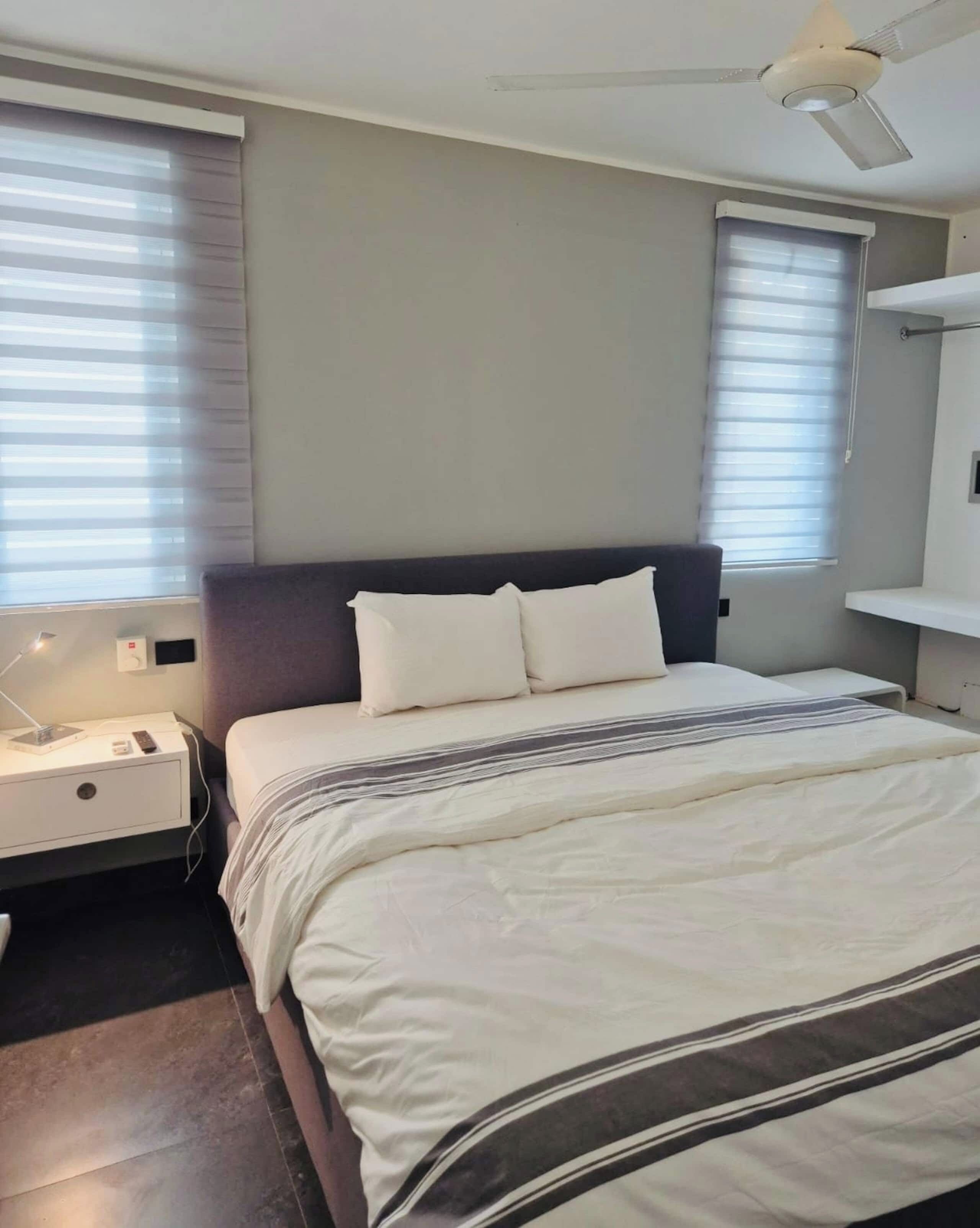 Quarto de hotel com cama, mesa de cabeceira, abajur e ventilador de teto.