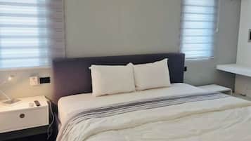 Quarto de hotel com cama, mesa de cabeceira, abajur e ventilador de teto.