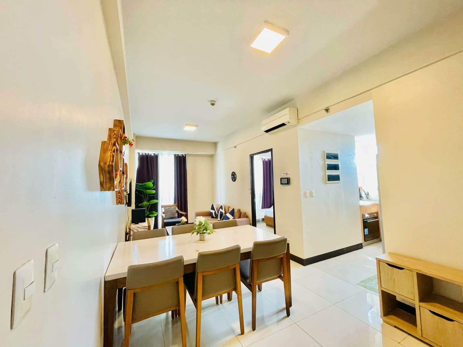 Uma sala de jantar moderna com uma mesa comprida e quatro cadeiras, um vaso de planta e um armário de madeira.