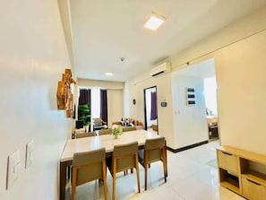 Uma sala de jantar moderna com uma mesa comprida e quatro cadeiras, um vaso de planta e um armário de madeira.