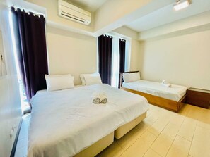 Quarto de hotel com uma cama grande, uma cama menor e uma mesinha de cabeceira.