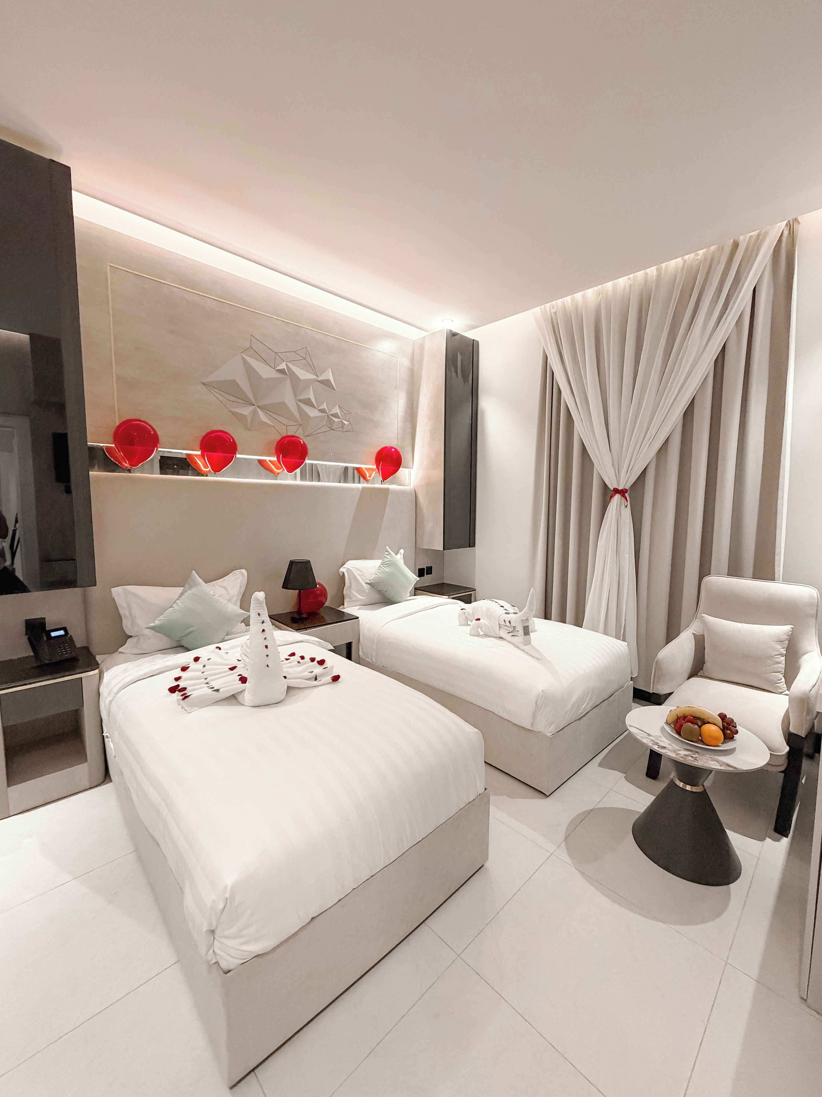 Quarto de hotel moderno com duas camas, um espaço para sentar e uma mesa de jantar com frutas.
