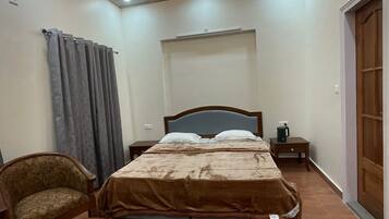 Quarto com cama, cadeira, mesa, ventilador de teto e janela com cortinas.
