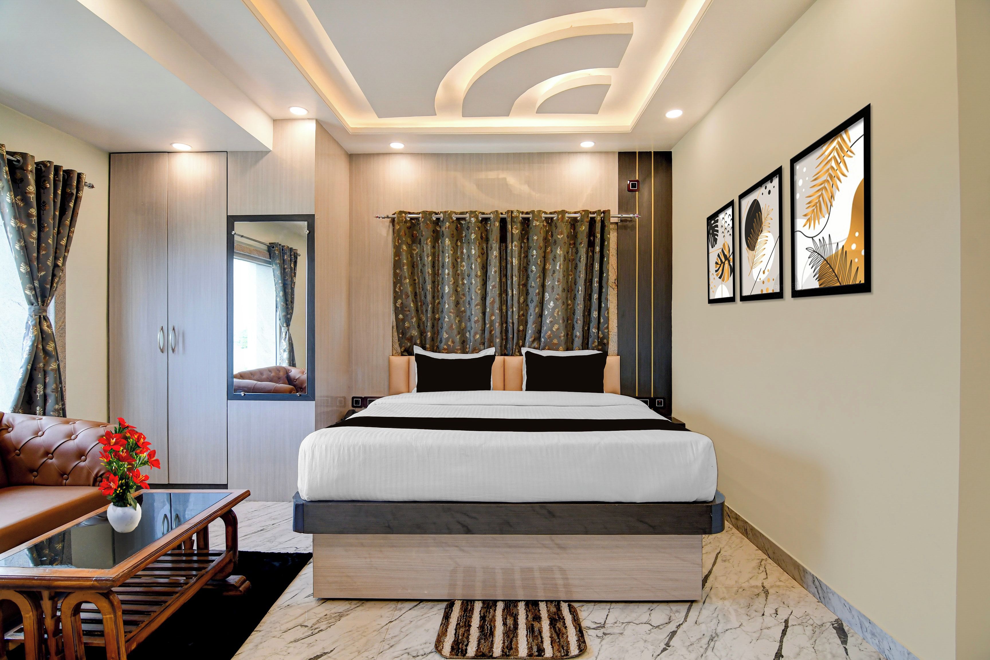 Quarto moderno com cama grande, área de estar com sofá e mesa, e um espelho decorativo.