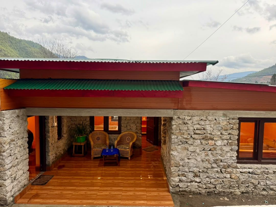 Edifício de pedra com piso de madeira e área externa coberta, com cadeiras e mesa.