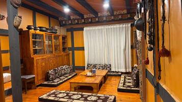 Quarto tradicional com piso de madeira, mesa de jantar, sofás e um armário.