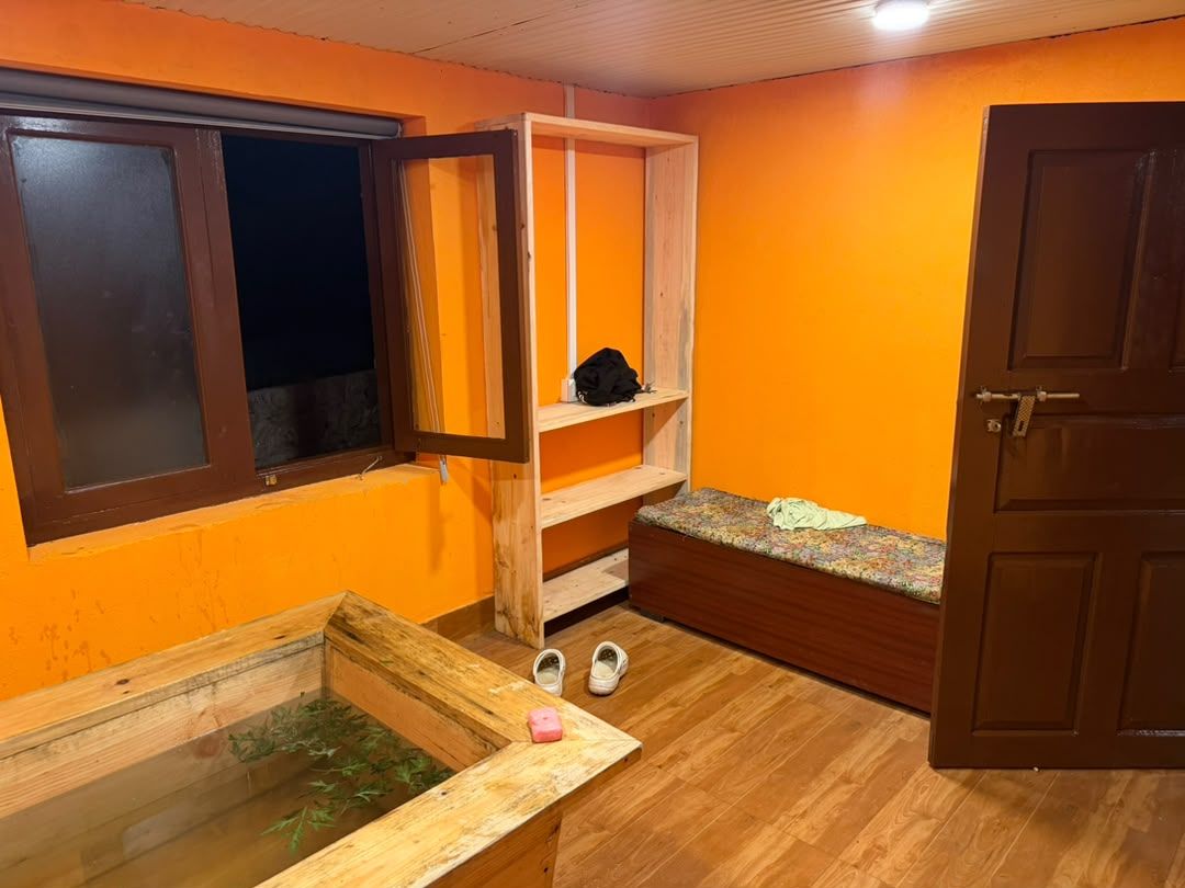 Quarto com um banco de madeira, uma pequena mesa com um objeto rosa e um par de sapatos.