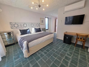 Quarto com cama, mesa de cabeceira e escrivaninha com cadeira.