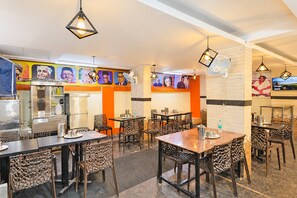 Um restaurante com várias mesas e cadeiras, uma área de cozinha e ventoinhas fixadas na parede.