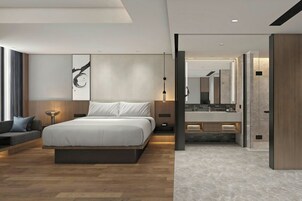Quarto moderno com uma cama grande, mesas de cabeceira, um criado-mudo, uma obra de arte na parede e vista para um banheiro.