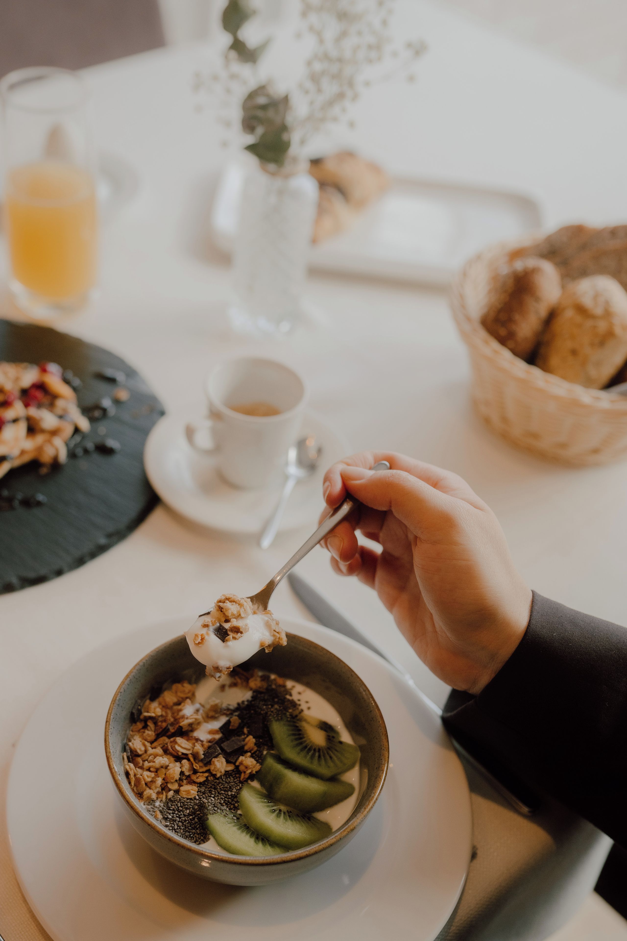 Mesa de café da manhã com tigela de cereal, fatias de kiwi e granola.