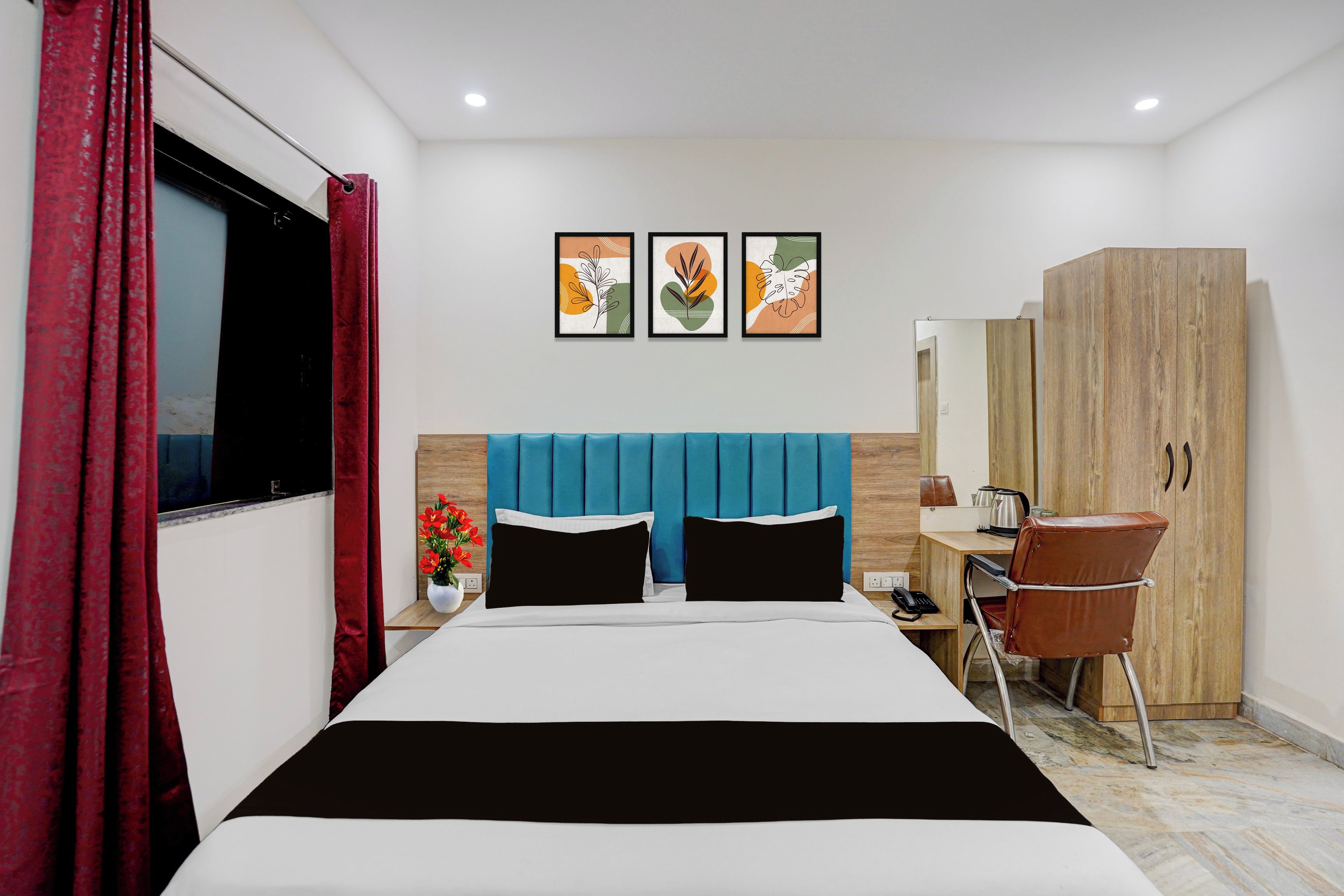 Quarto de hotel com uma cama, escrivaninha, cadeira, guarda-roupa e três quadros na parede.