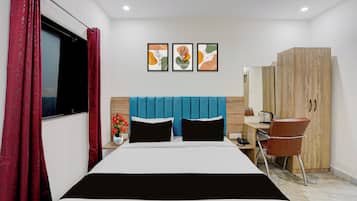 Quarto de hotel com uma cama, escrivaninha, cadeira, guarda-roupa e três quadros na parede.