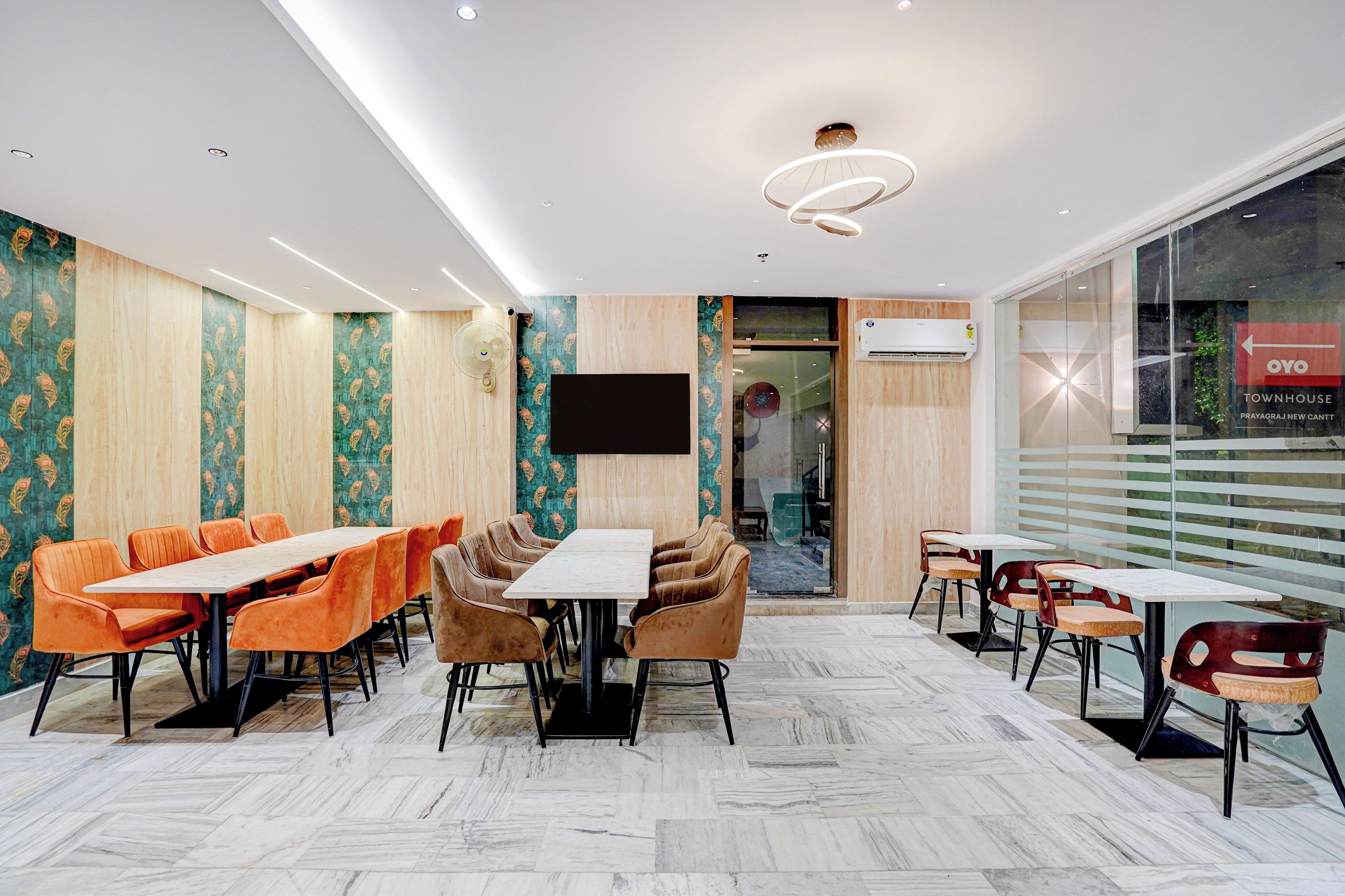 Uma área de refeições moderna, com uma mesa comprida, várias cadeiras, um ar condicionado e vista para o exterior.