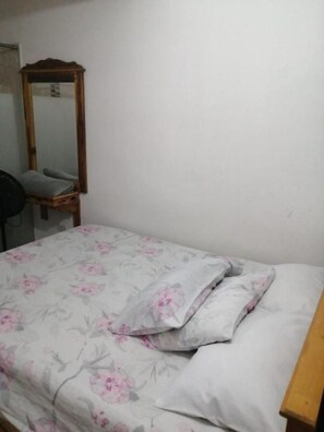 Quarto com uma cama de solteiro, cabeceira de madeira, mesa de cabeceira e espelho na parede.
