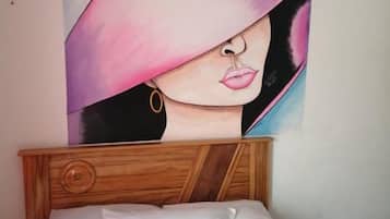 Cama com lençóis brancos, um controle remoto sobre a cama e uma grande pintura abstrata acima.