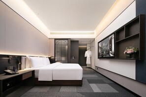 Quarto de hotel moderno com uma cama bem arrumada, mesa de cabeceira com abajur, espelho grande e televisão de tela plana.