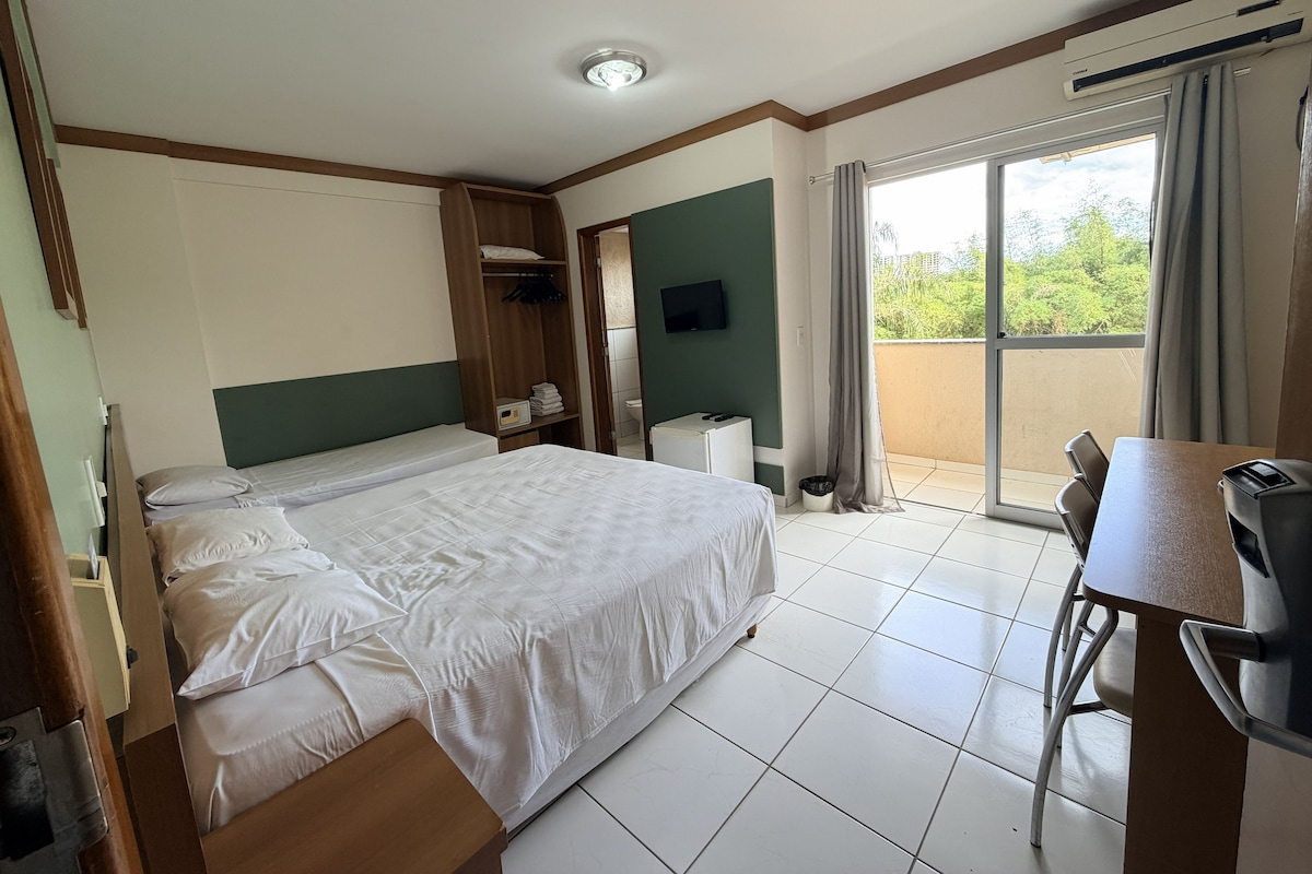 Quarto de hotel com cama, escrivaninha, cadeira, televisão e varanda com vista.