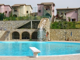 Piscina com cachoeira, paredes de pedra e uma série de arcos.