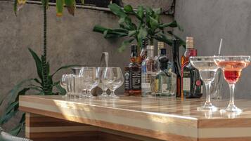 Uma área de bar com banquetas, balcão e diversos copos e garrafas.