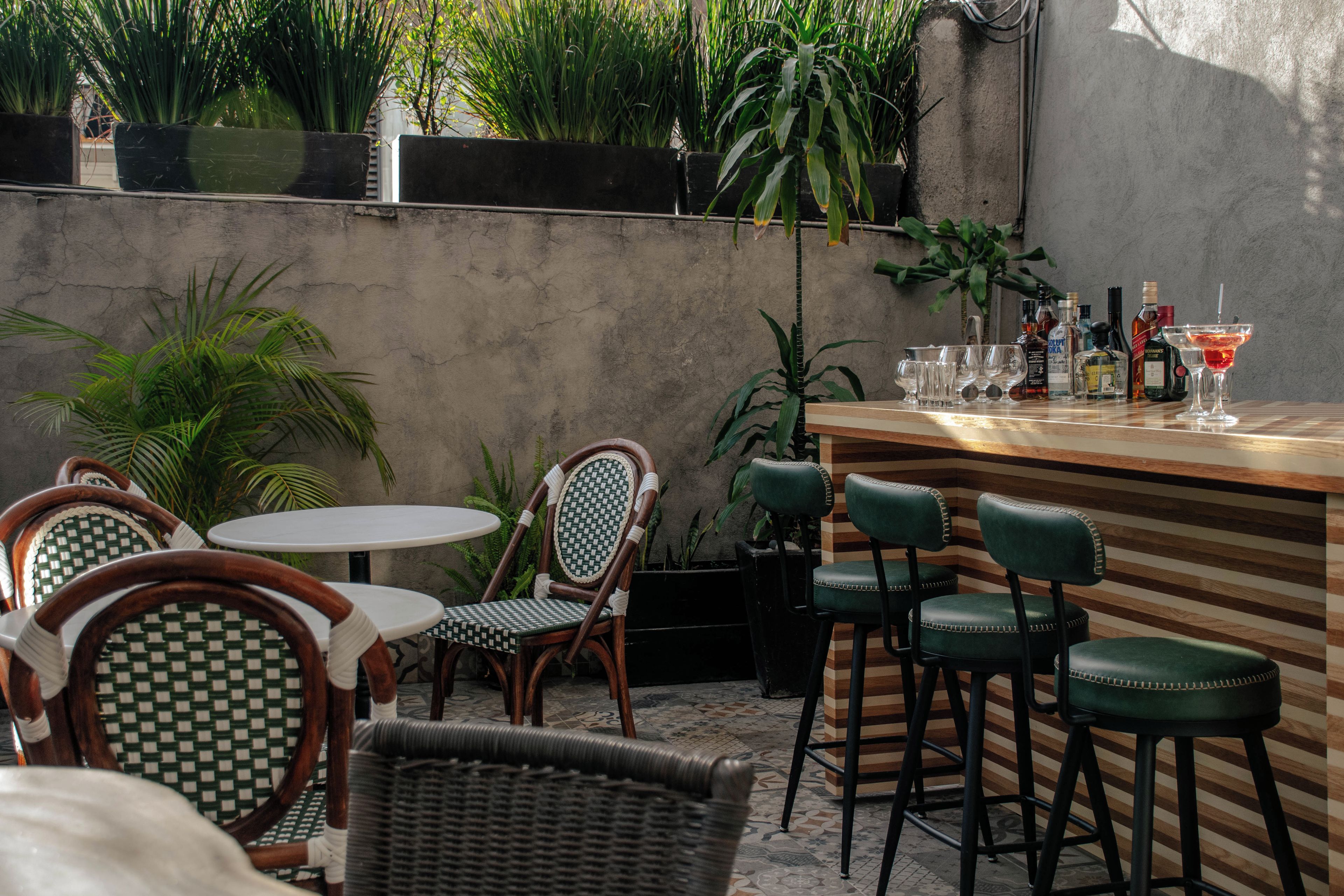 Espaço ao ar livre com área de estar, cadeiras de vime e um bar com diversas garrafas e copos.