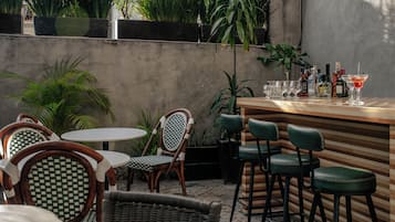 Espaço ao ar livre com área de estar, cadeiras de vime e um bar com diversas garrafas e copos.