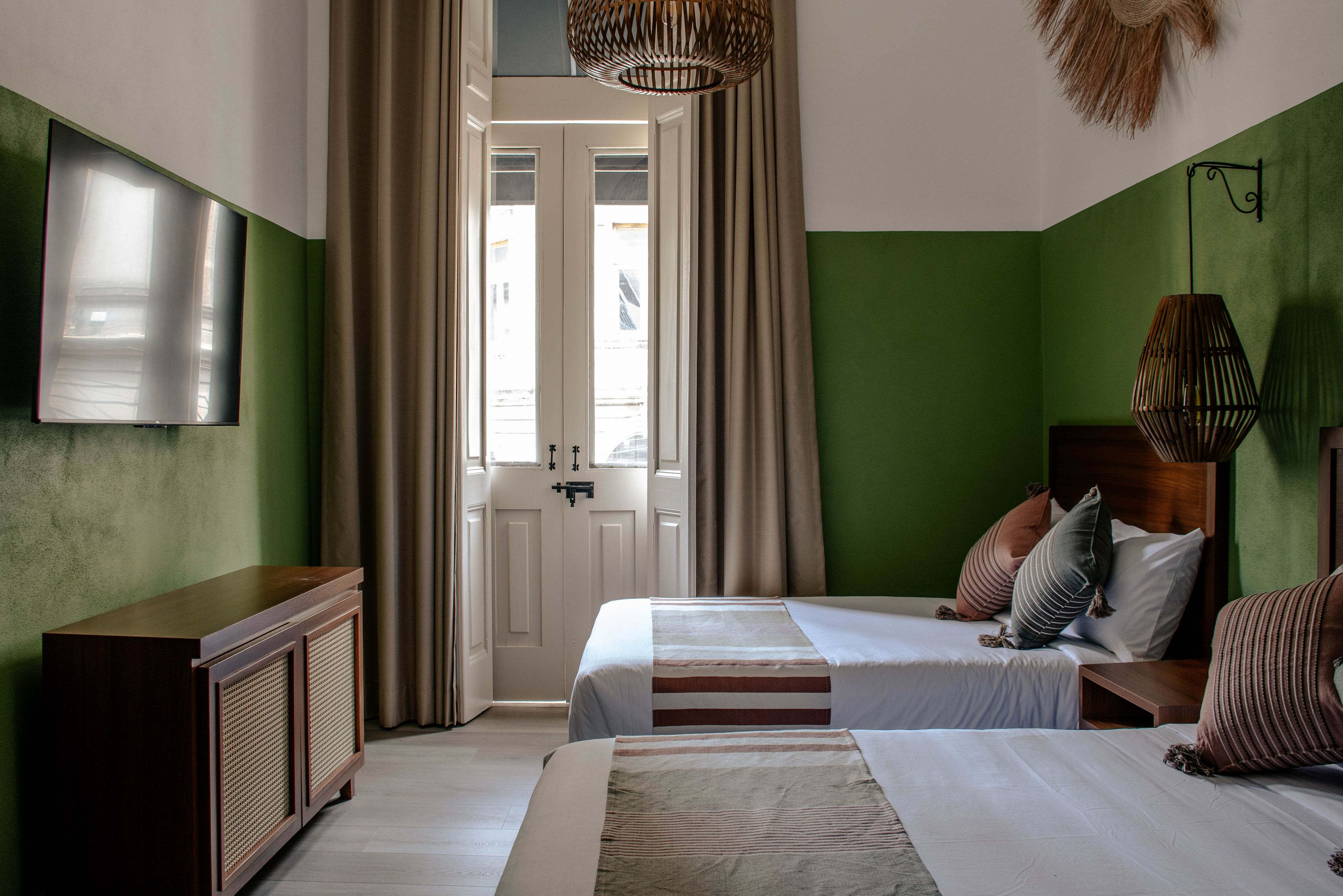 Quarto de hotel com duas camas, televisão, um armário de madeira e parede verde.