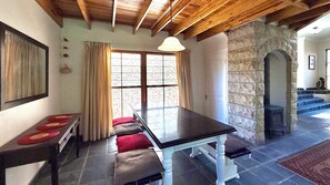 Uma área de refeições com mesa e bancos, parede de pedra e escada que leva a um andar superior.