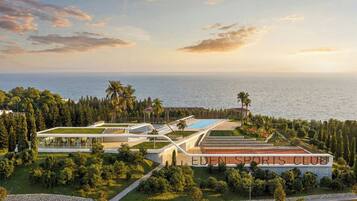 Um clube esportivo moderno com piscina, quadras de tênis e vista para o mar.
